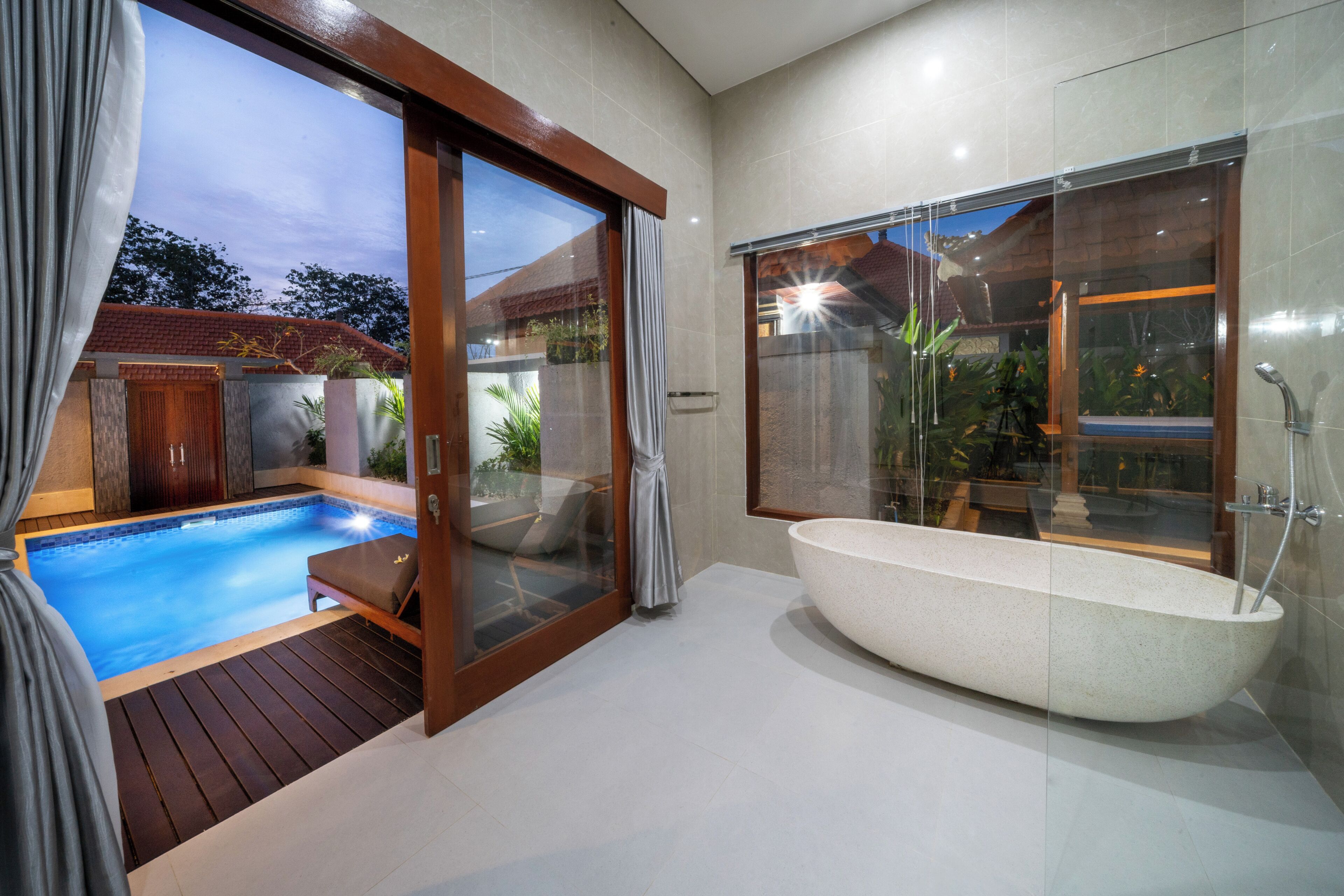 Um banheiro moderno com uma banheira independente, chuveiro com box de vidro e uma piscina visível através das portas de vidro.