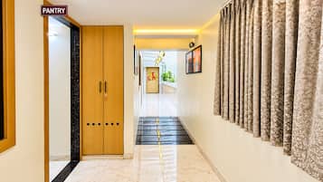 Um corredor com porta de madeira identificada como 'PANTRY', um letreiro com a palavra 'WELCOME' e cortinas estampadas.