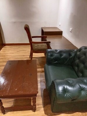 Um quarto com piso de madeira, uma cadeira de madeira, um sofá de couro e uma mesa de madeira.