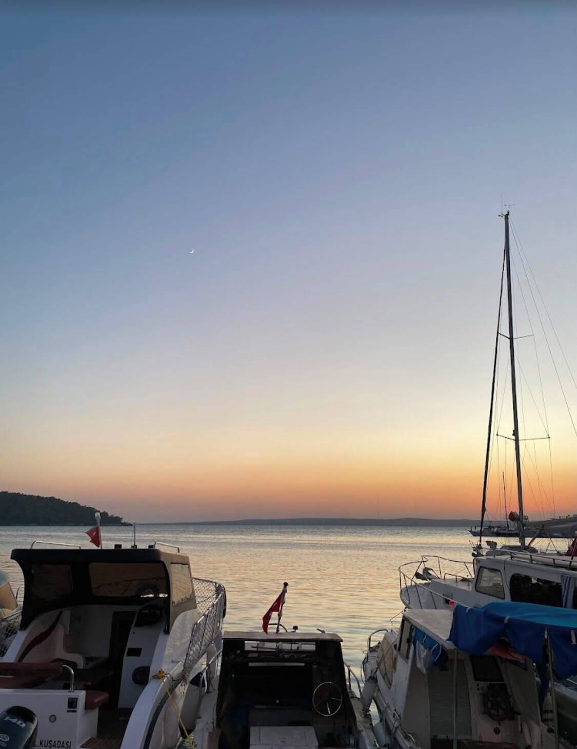 Uma marina com barcos atracados, céu claro e mar calmo.