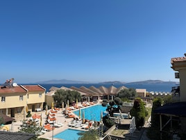 Um resort com piscina, cadeiras de descanso e vista para o mar e montanhas ao longe.