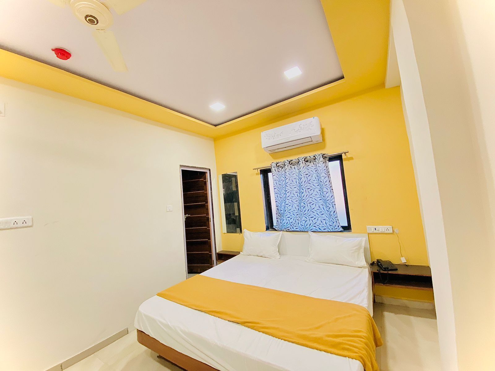 Quarto com cama, ar condicionado, janela com cortina estampada e guarda-roupa.