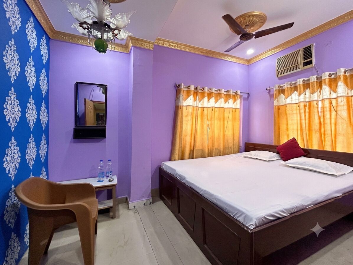 Quarto com cama, escrivaninha, cadeira, ventilador de teto e janela com cortinas.