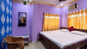 Quarto com cama, escrivaninha, cadeira, ventilador de teto e janela com cortinas.