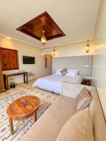 Quarto de hotel com cama, sofá, escrivaninha, televisão e teto com decoração.