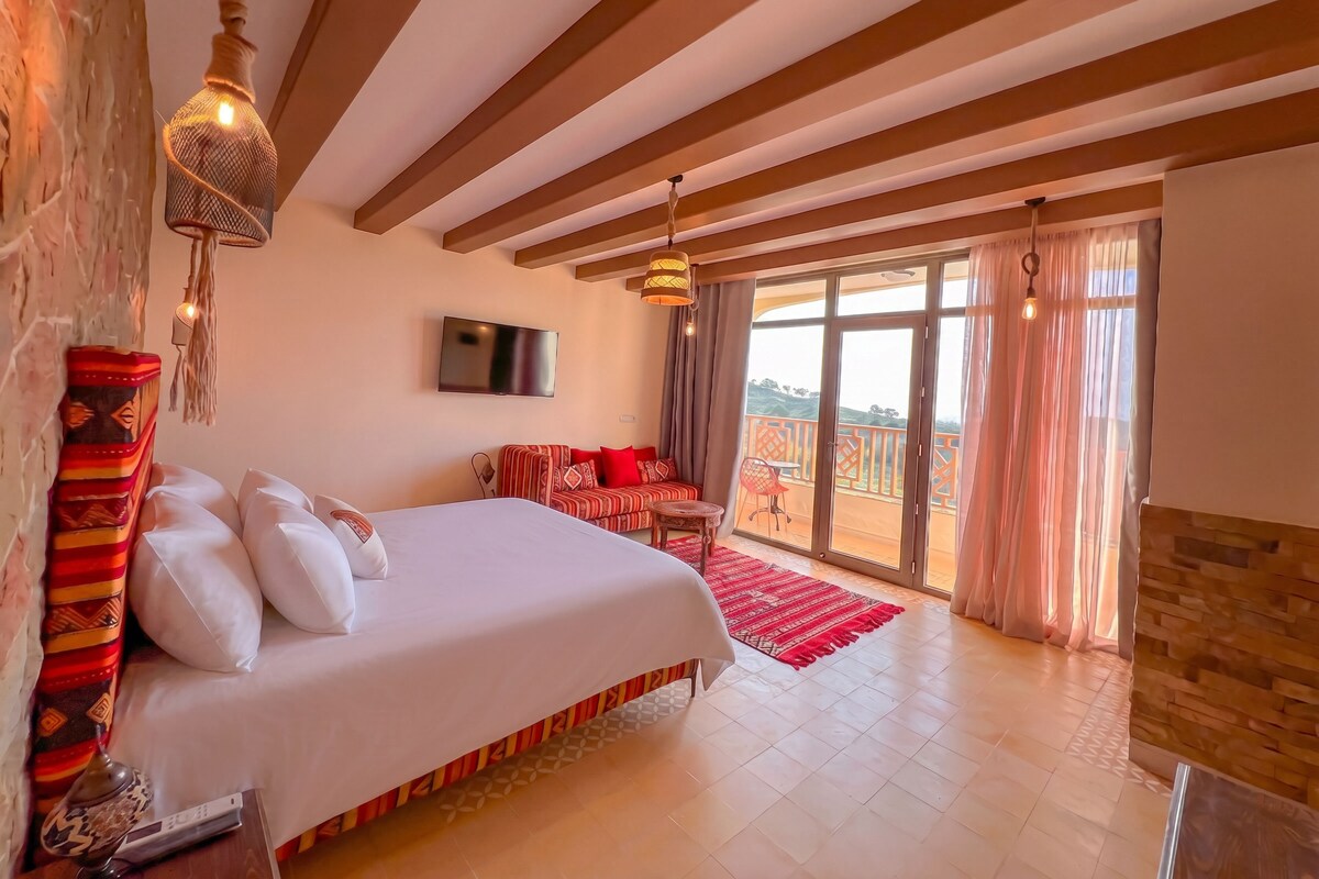 Um quarto com uma cama, televisão, varanda e parede de pedra.