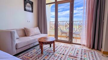Quarto com sofá, mesa redonda pequena, tapete estampado e varanda com vista.