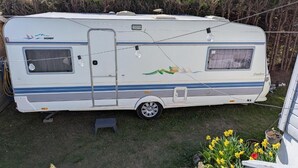 Uma caravana branca para lazer, com uma porta lateral, uma pequena janela e um desenho decorativo na lateral.