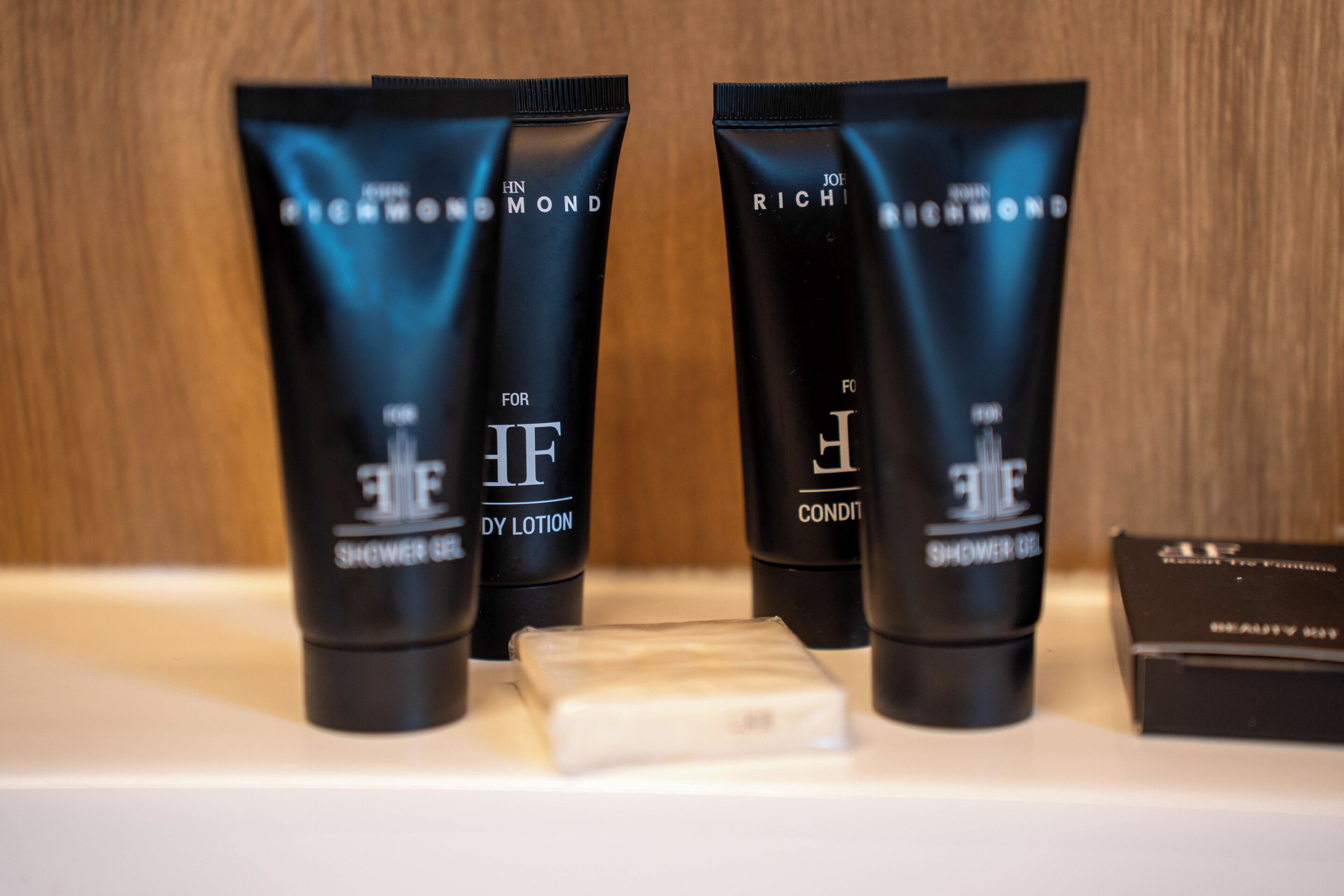 Uma prateleira com tubos pretos identificados como 'IF SHOWER GEL' e 'IF SHOWER GLO', uma barra de sabão e uma caixa preta.