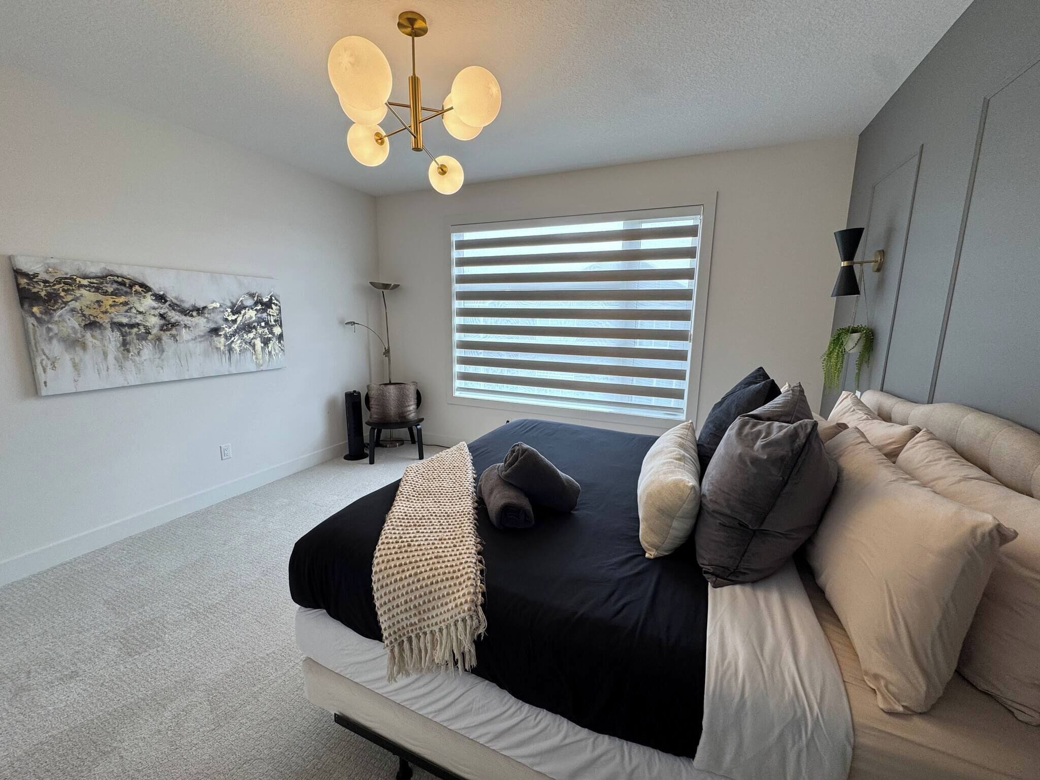 Quarto com cama, luminária de chão, janela com persianas e uma obra de arte na parede.