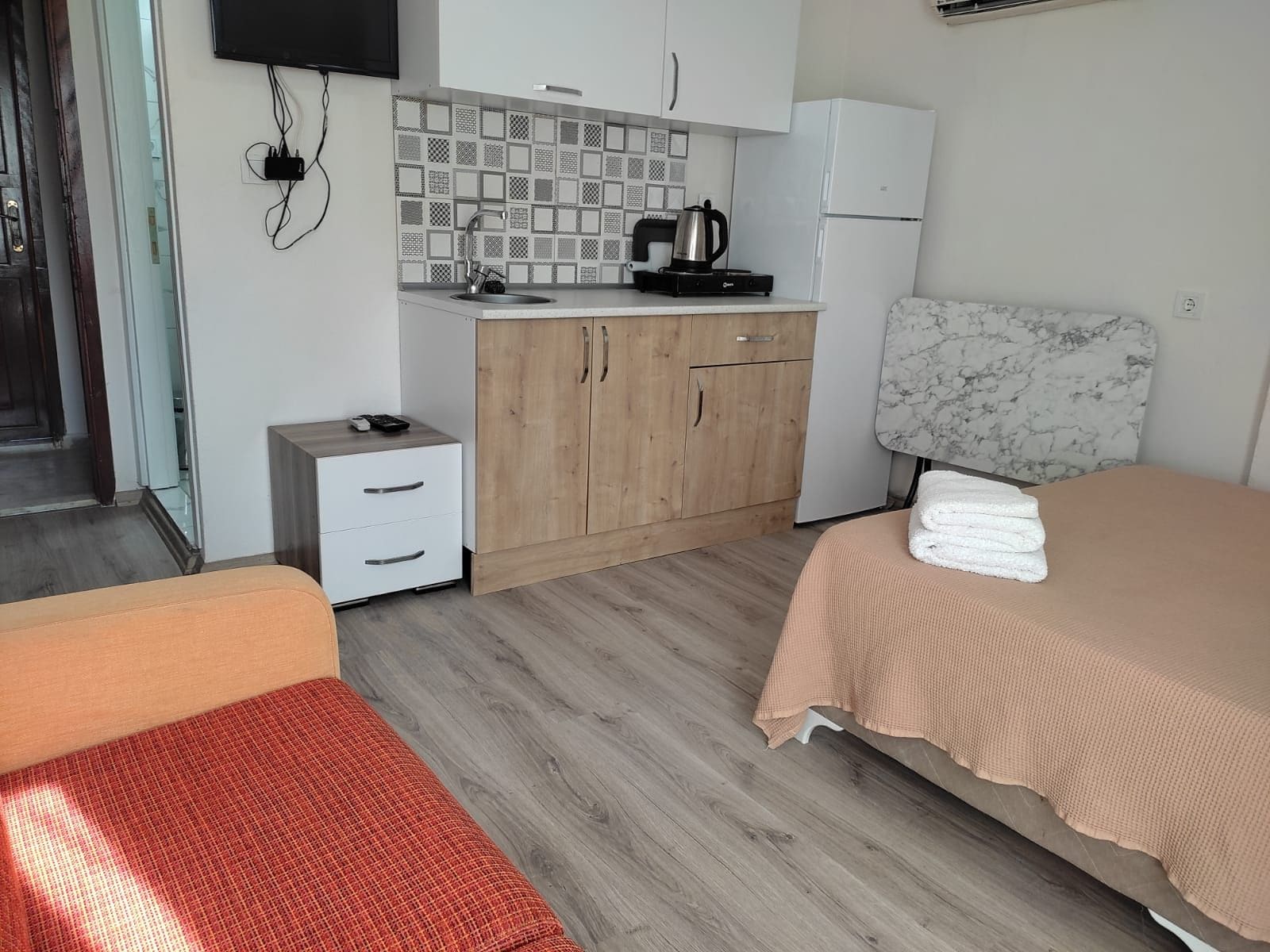 Quarto de hotel compacto com cozinha compacta, cama com cabeceira de mármore, área de estar pequena e vista por uma porta de vidro.