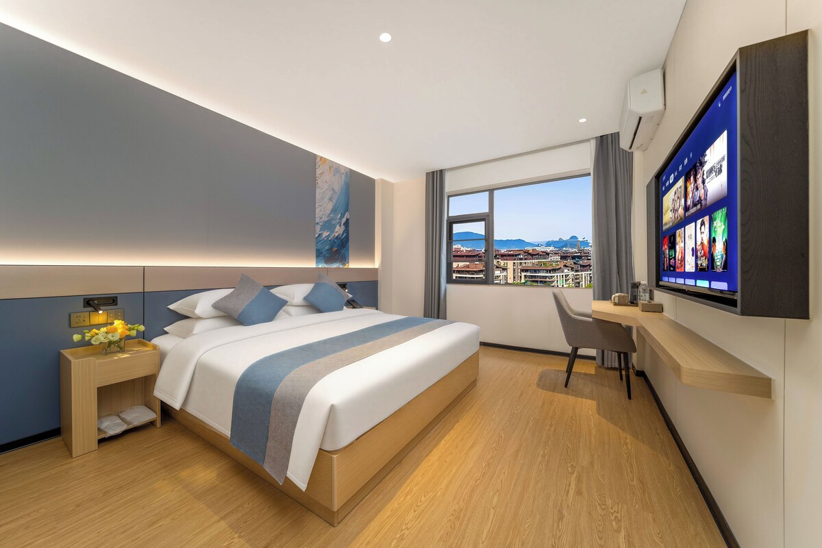 Quarto de hotel moderno com uma cama grande, uma escrivaninha e uma televisão.