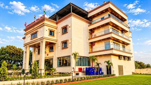 Um hotel com vários andares, entrada imponente, colunas e uma placa com a inscrição 'Sundaram Palace'.
