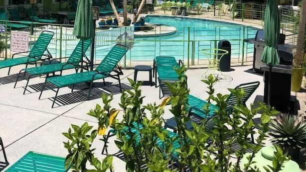 Uma área de piscina com espreguiçadeiras e guarda-sóis, cercada por um edifício com vários andares e varandas.