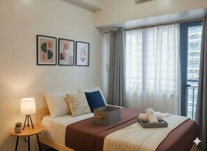 Quarto de hotel com uma cama, uma mesa de cabeceira com abajur, uma pequena planta e uma janela com cortinas.