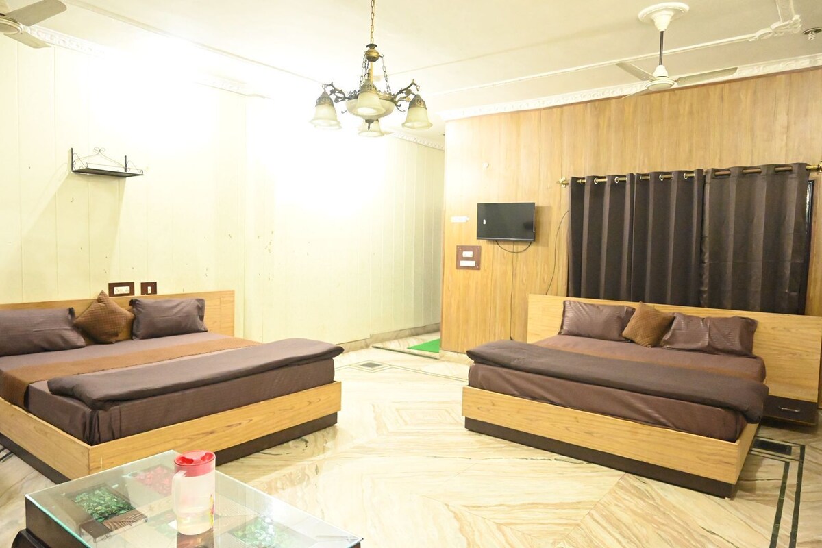 Quarto com duas camas de madeira, uma mesa de centro de vidro, um ventilador de teto e uma televisão montada.
