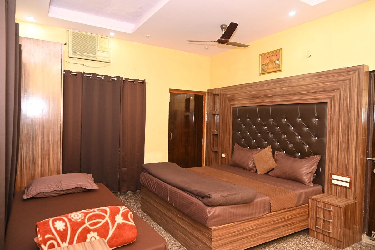 Quarto com uma cama grande, um sofá menor, um armário de madeira, um ventilador de teto e uma janela com cortinas.