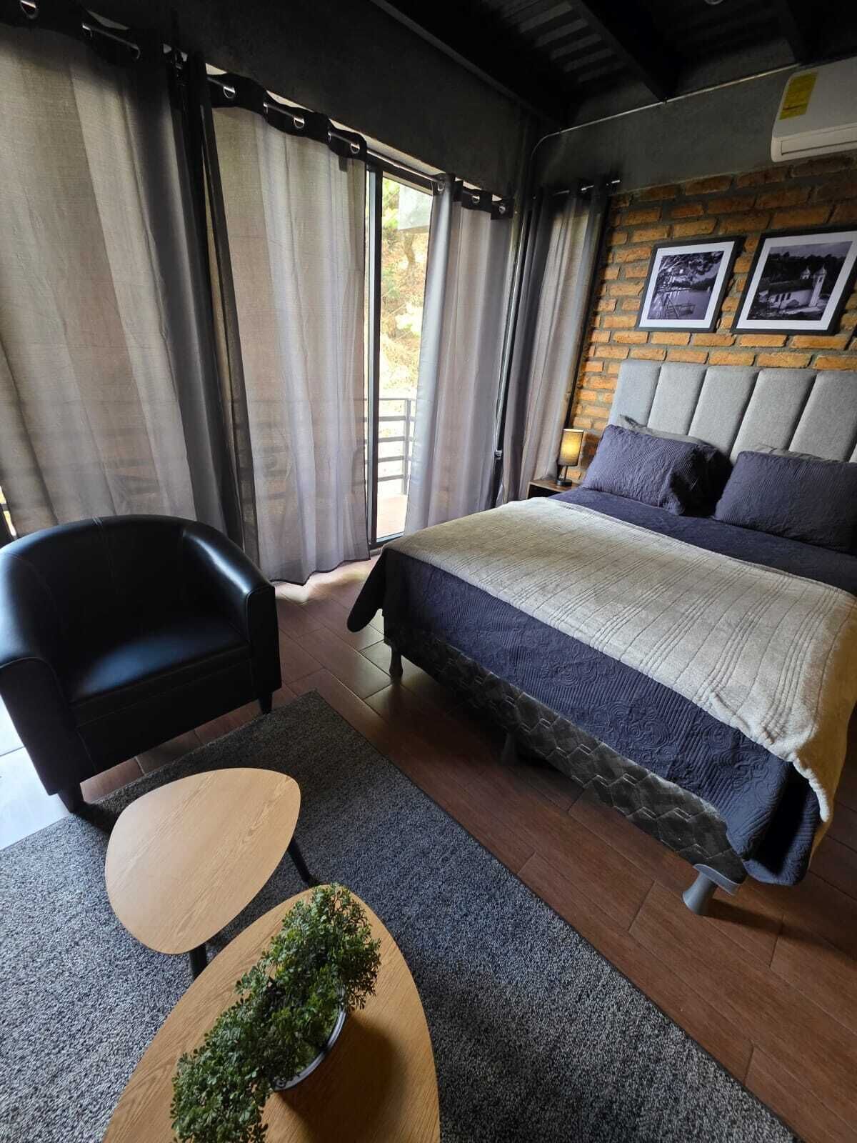 Quarto com cama, uma cadeira, mesa pequena e planta em vaso.