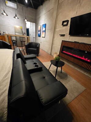 Uma sala de estar moderna com um sofá modular preto, uma mesinha redonda, uma televisão de tela plana na parede e uma lareira embutida.