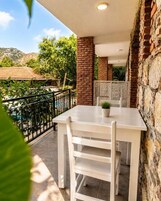 Mesa e cadeiras brancas numa varanda com parede de tijolos e vista para montanha e árvores.