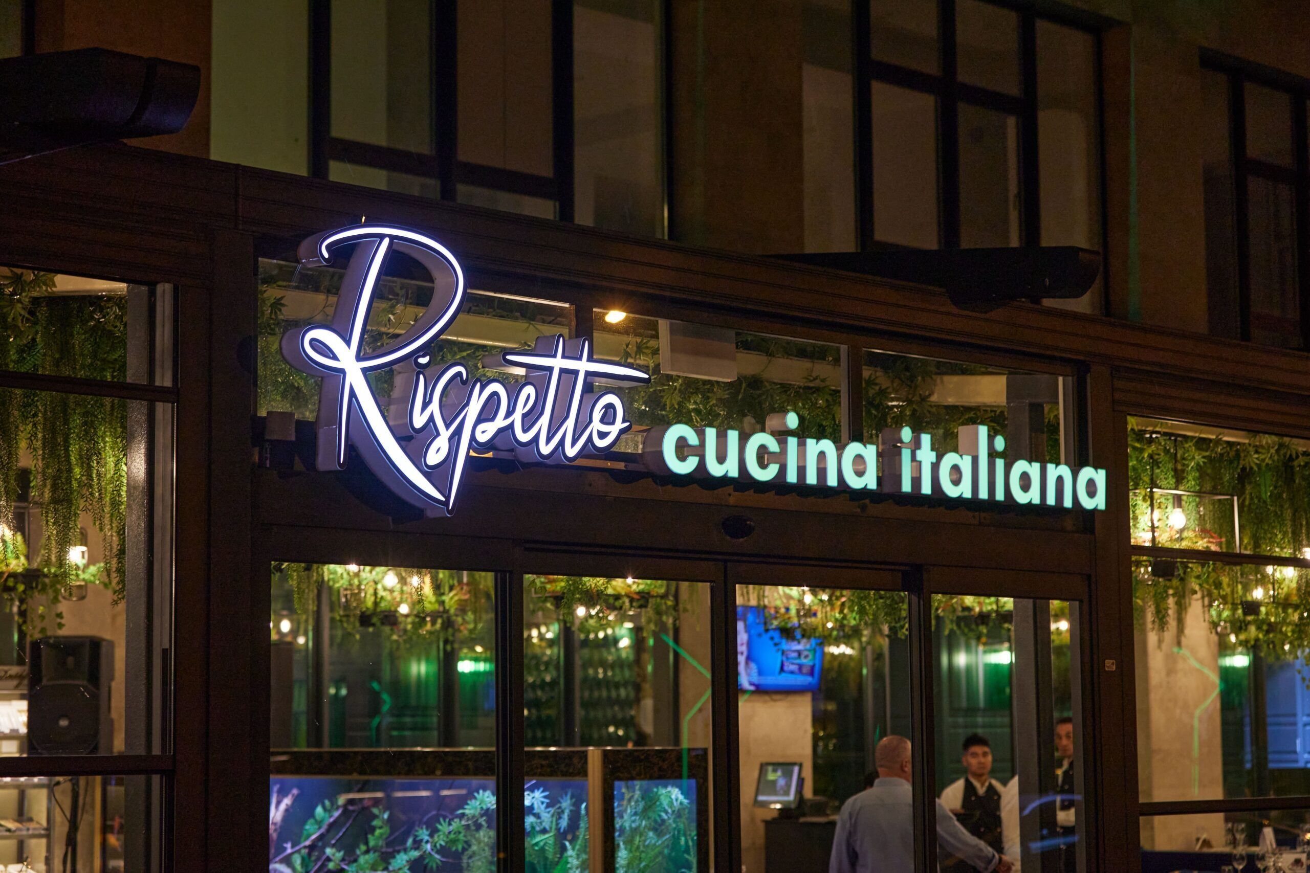 Um restaurante chamado 'Ristorante cucina italiana', com letreiro de neon, amplas janelas e plantas em vasos.