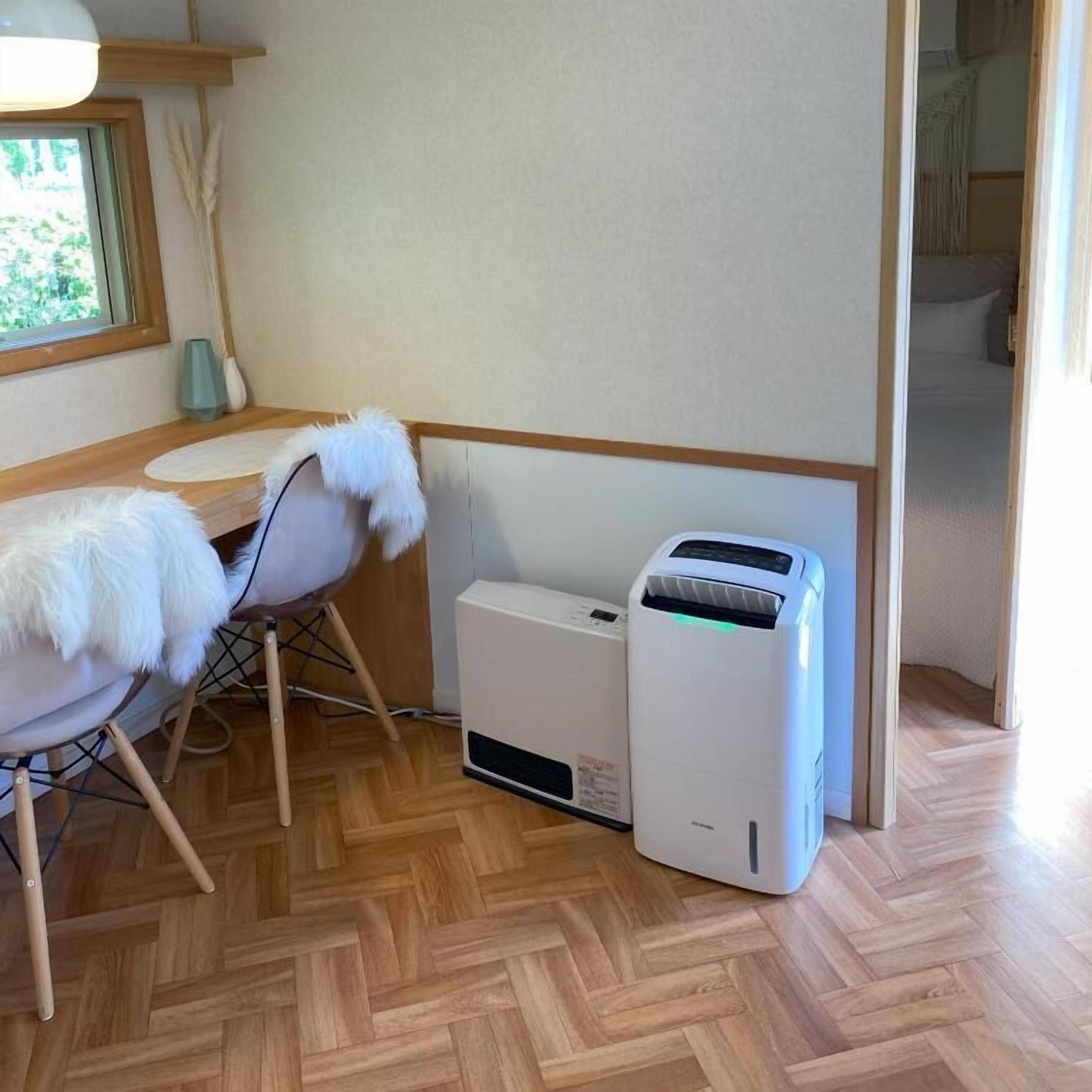 Quarto com piso de madeira, uma cadeira branca com almofada macia, uma mesa pequena e um ar-condicionado branco.