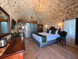 Quarto com teto de pedra, cama com roupa de cama verde e branca, escrivaninha de madeira e uma cadeira.