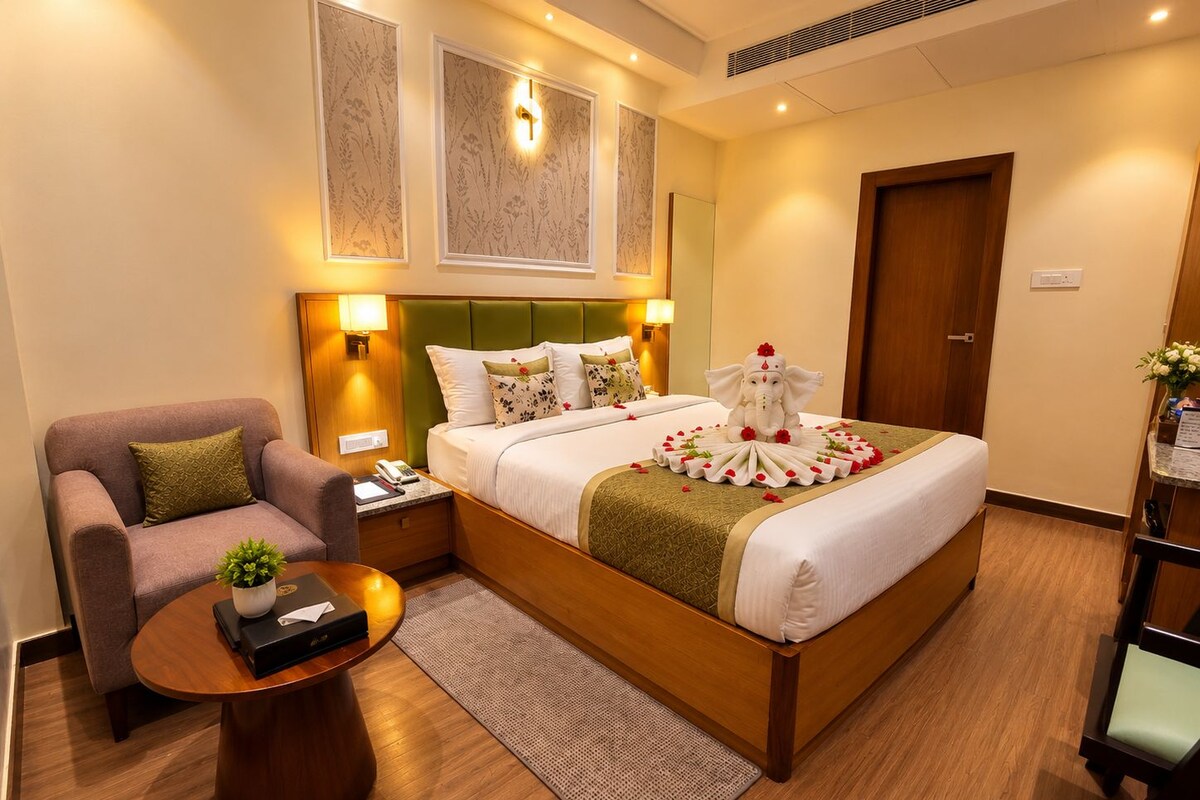 Quarto de hotel com cama, uma cadeira, uma mesinha e um enfeite de elefante decorativo.