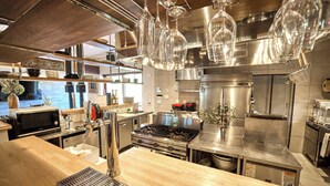 Cozinha moderna com eletrodomésticos de aço inoxidável, bancadas de madeira e taças de vinho penduradas.