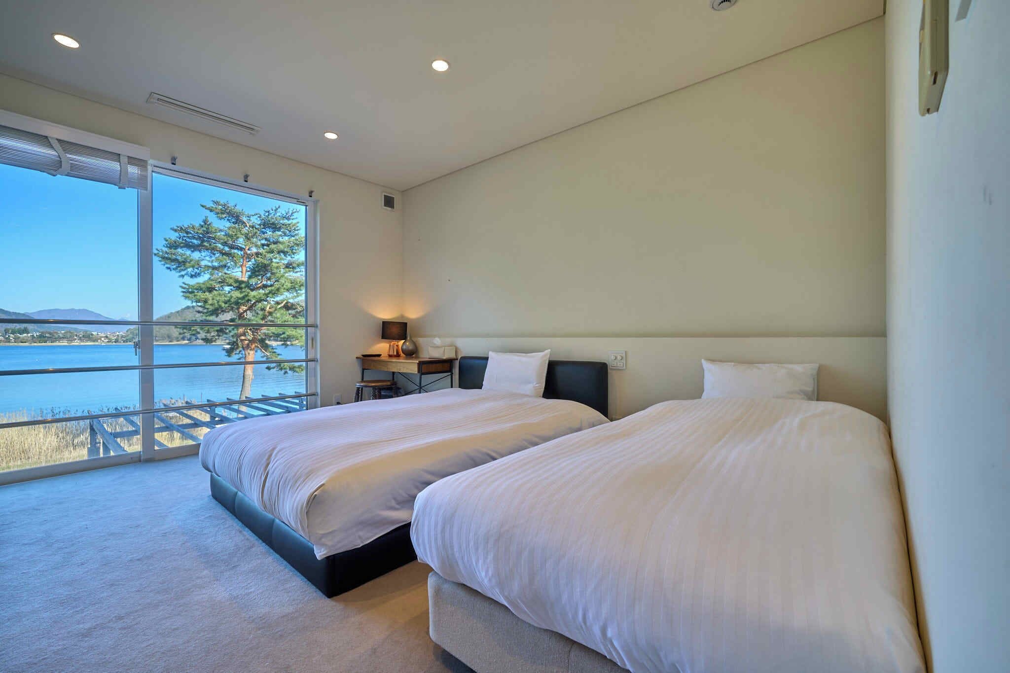 Quarto com duas camas, uma escrivaninha e uma grande janela com vista para a água.