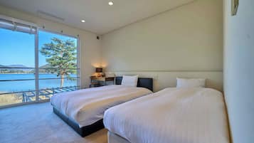 Quarto com duas camas, uma escrivaninha e uma grande janela com vista para a água.