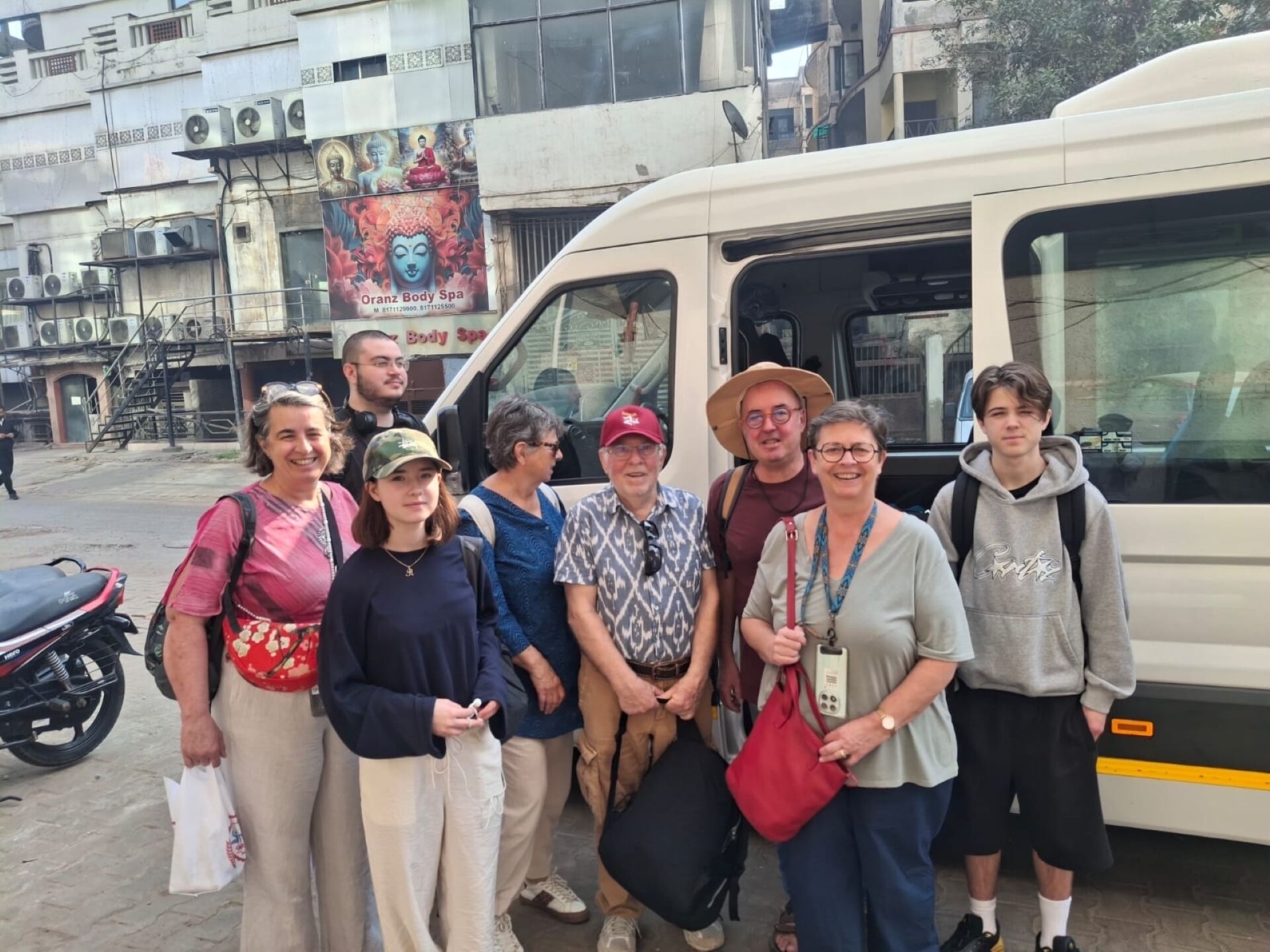Um grupo de pessoas em frente a um ônibus, com um edifício ao fundo.