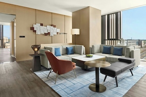 Quarto de hotel moderno com sofá, mesa de centro, mesinha de cabeceira com abajur e um objeto decorativo na parede.