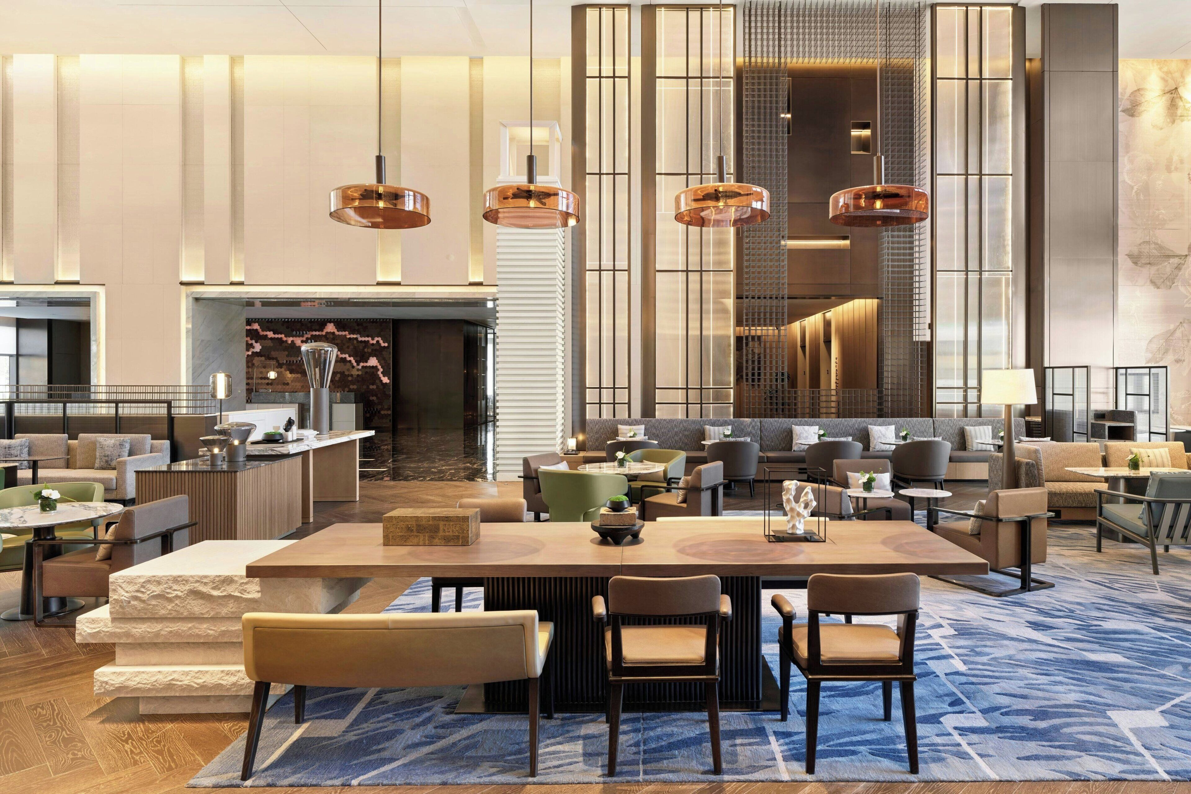 Um hall de hotel moderno com área de estar central, um bar e um grande painel decorativo.