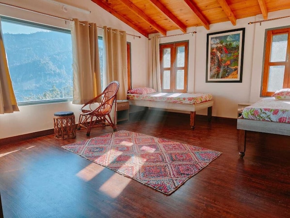 Quarto com cama, poltrona, mesinha e janela com vista para montanhas.