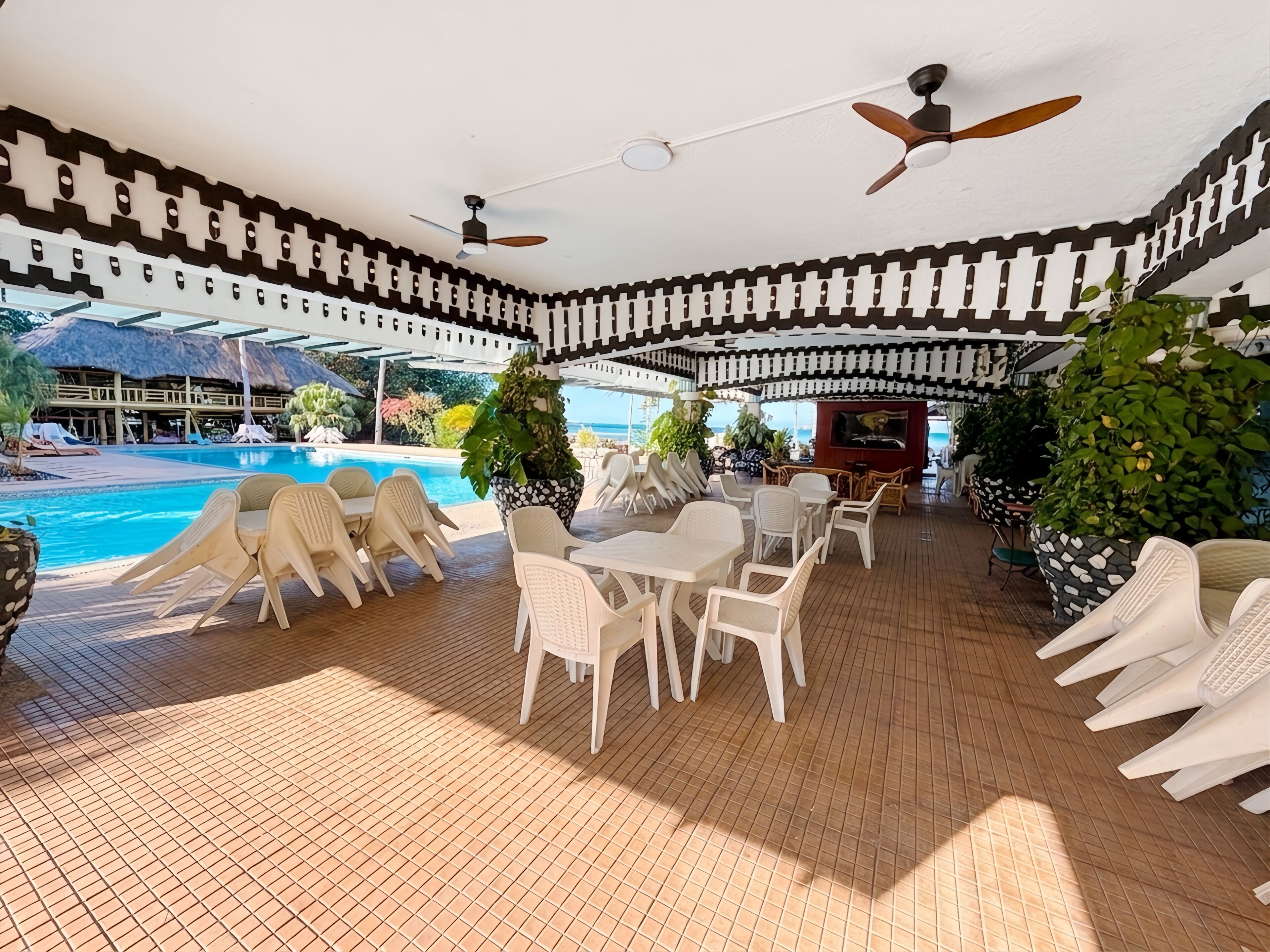 Uma área externa coberta com piscina, espreguiçadeiras e mesas.
