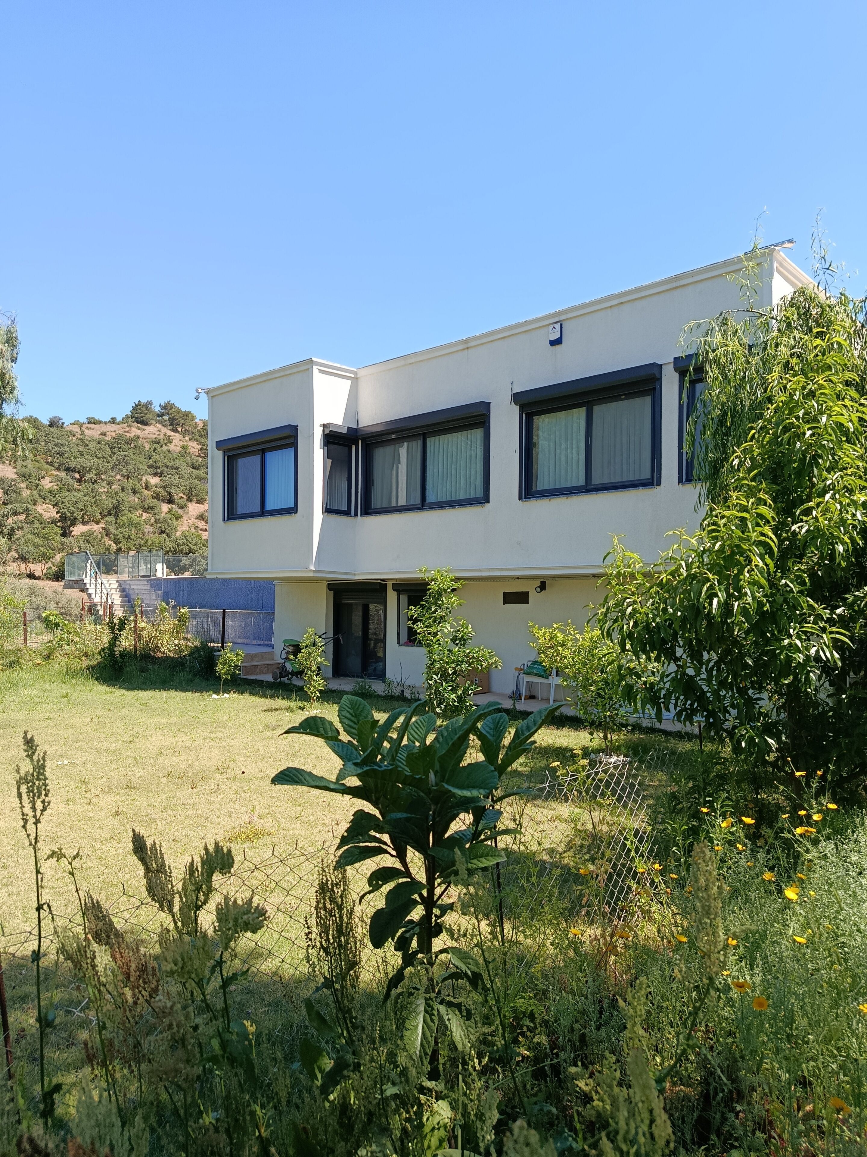 Uma casa moderna de dois andares com telhado plano, janelas amplas e um jardim bem cuidado.