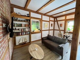Um quarto aconchegante com teto de madeira, estante de livros, sofá, mesa redonda e janela com vista para o verde.