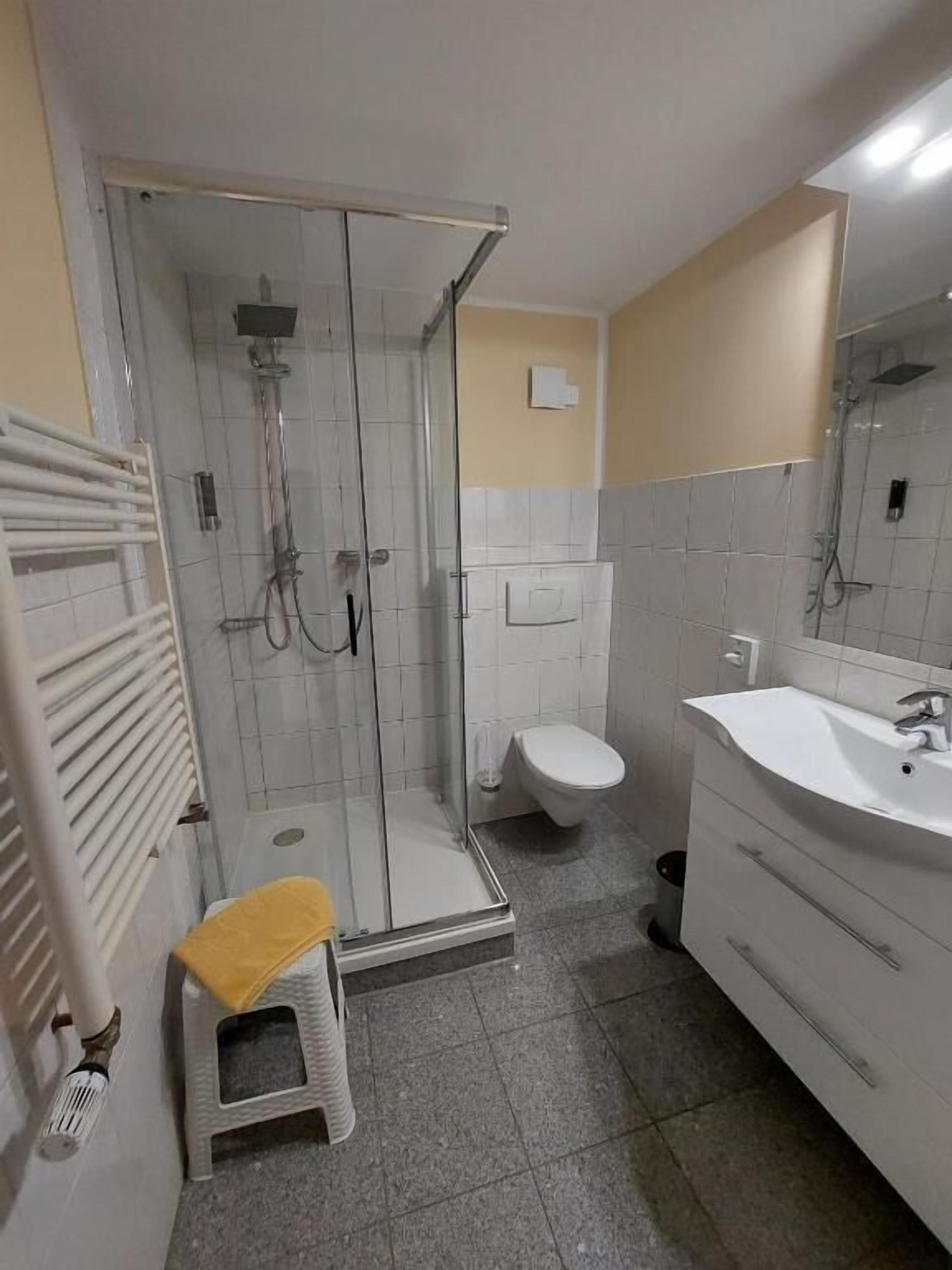 Casa de banho com cabine de chuveiro em vidro, sanita e lavatório com espelho.