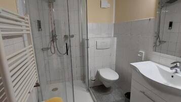 Casa de banho com cabine de chuveiro em vidro, sanita e lavatório com espelho.