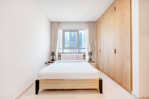 Quarto com cama grande, guarda-roupa, mesa de cabeceira com luminária e janela com cortinas.