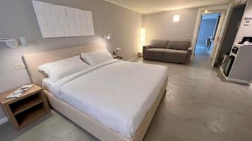 Quarto de hotel moderno com uma cama grande, um sofá, uma mesa pequena e uma obra de arte na parede.