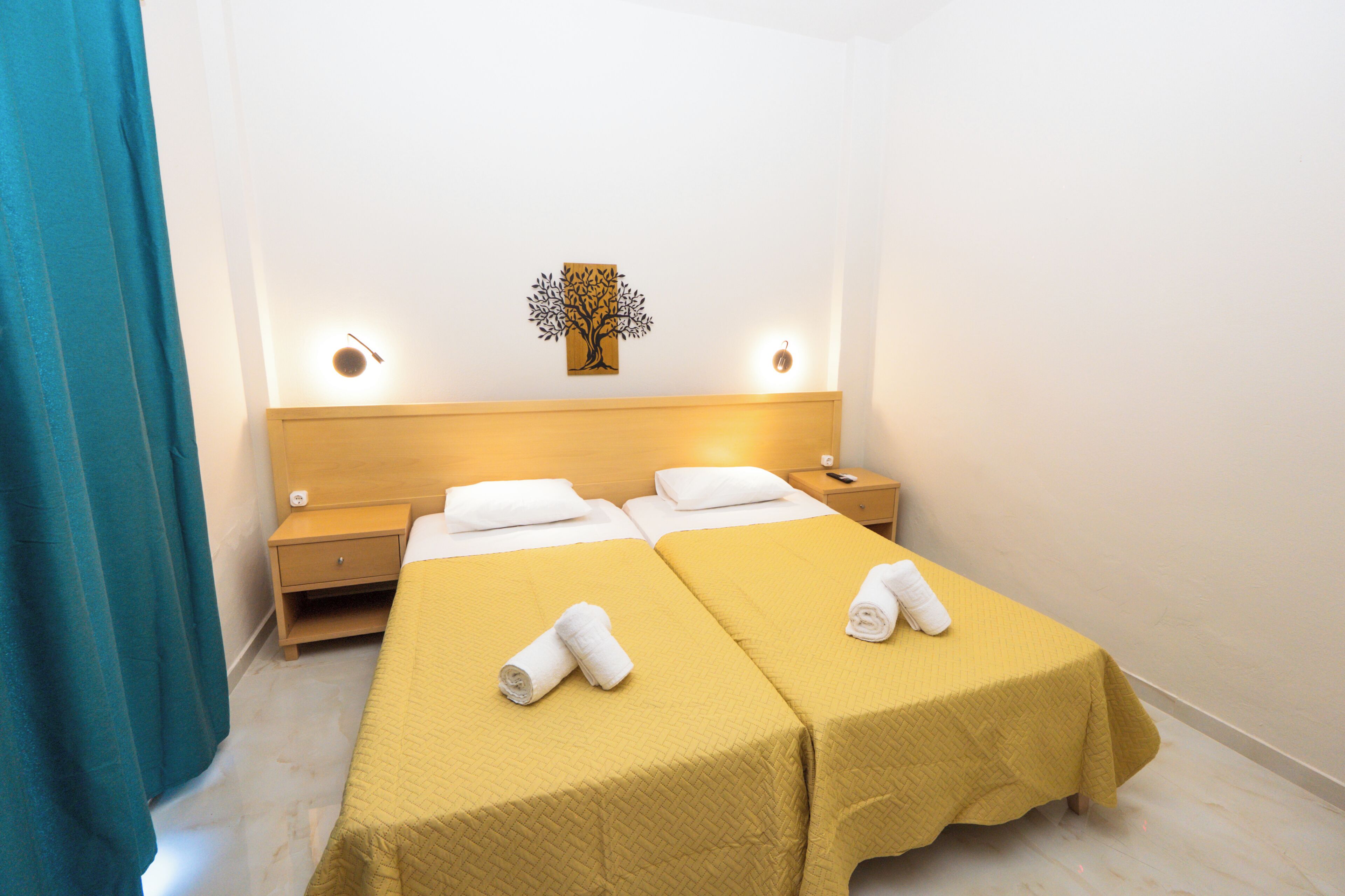 Quarto de hotel com duas camas, uma mesa de cabeceira, uma luminária na parede e uma obra de arte na parede.