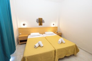 Quarto de hotel com duas camas, uma mesa de cabeceira, uma luminária na parede e uma obra de arte na parede.