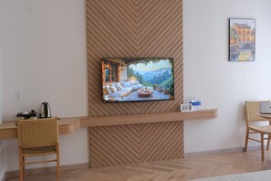 Quarto moderno com televisão de tela plana presa a uma parede de madeira, uma cadeira de vime, um laptop sobre uma mesinha e um quadro emoldurado.
