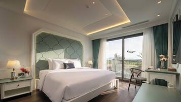 Quarto de hotel moderno com uma cama grande, uma mesa e vista para um avião decolando.