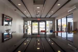 Um hall de hotel moderno com piso refletivo, balcão de recepção e vista para o exterior.
