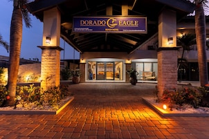Entrada do Hotel Dorado Eagle Beach, com um caminho de tijolos que leva às portas, palmeiras e uma placa sobre a entrada.