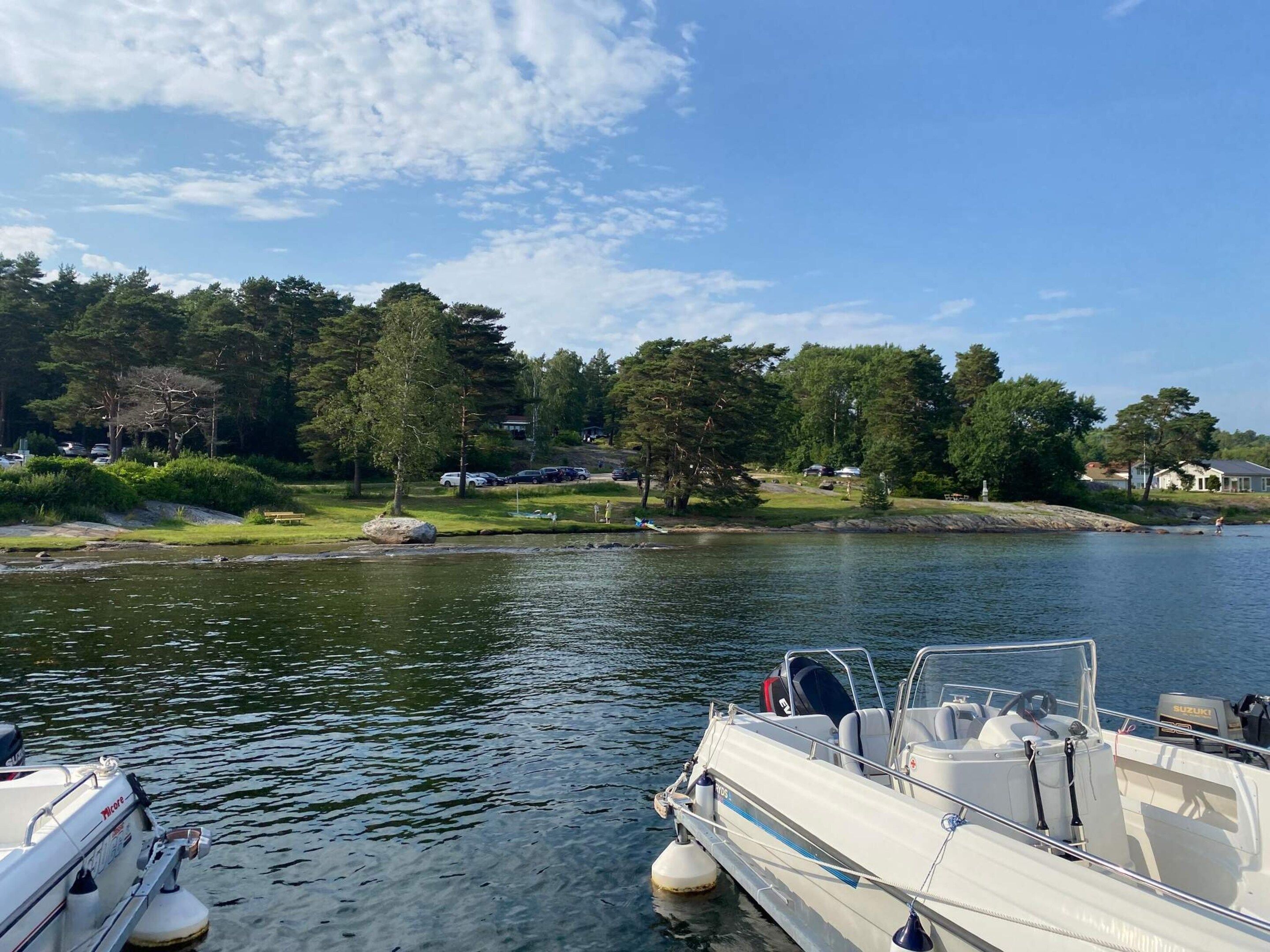 Um lago com um barco atracado à direita, cercado por árvores e algumas casas ao fundo.