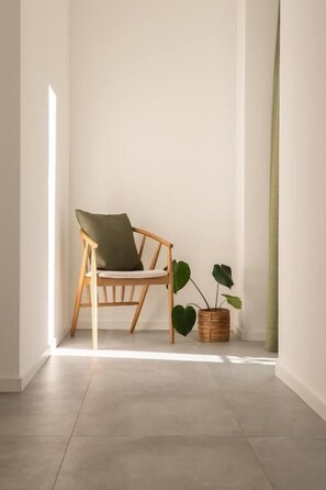Quarto de canto com cadeira de madeira, almofada verde e planta em vaso.